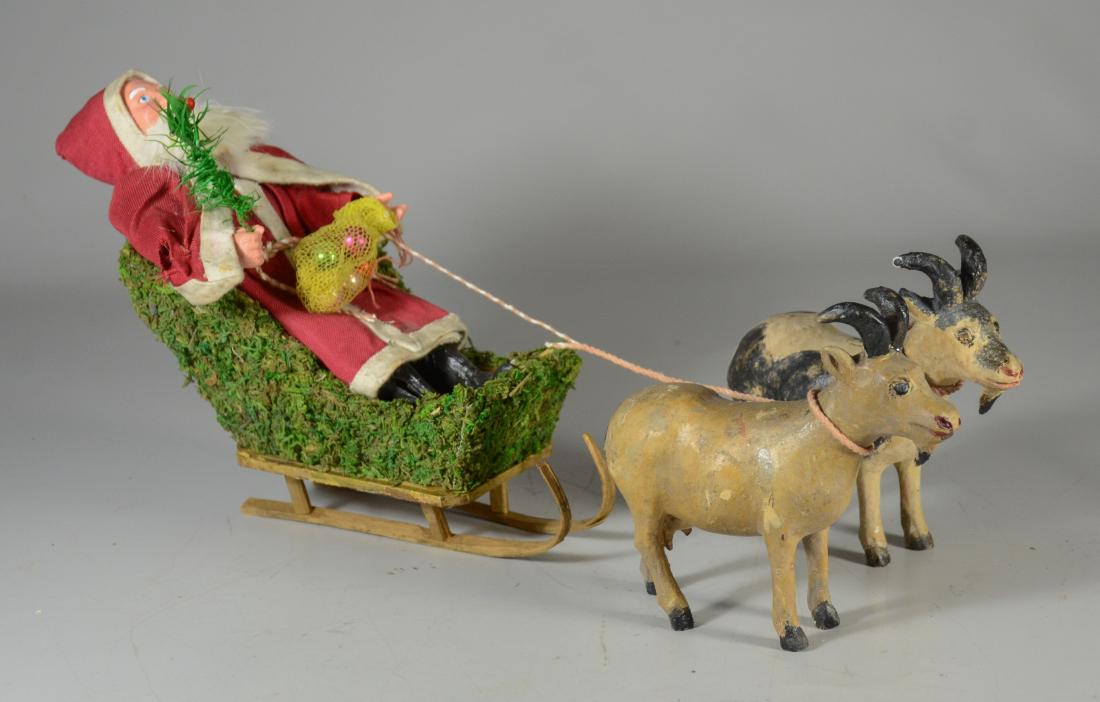 Santa Claus, long red coat riding in goat drawn sleigh
